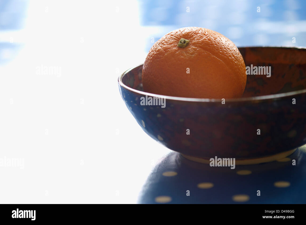 A single orange in a bowl on table Stock Photo - Alamy