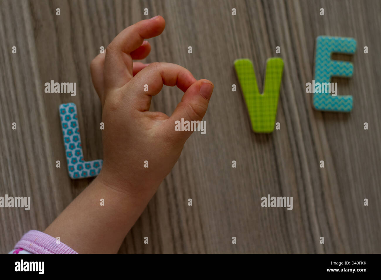 Child is writing word love with colourful toy letters on a wooden ...