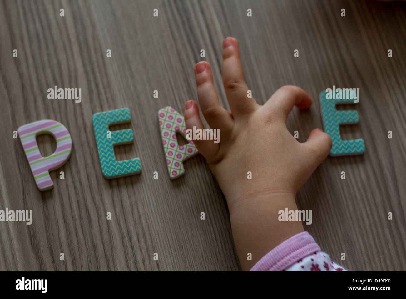 Child is writing word peace with colourful toy letters on a wooden ...