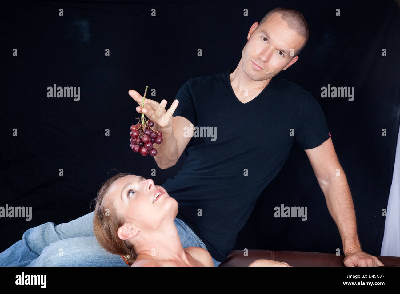 Cute romantic couple feeding each other grapes. He is hanging the grapes over her mouth and ...