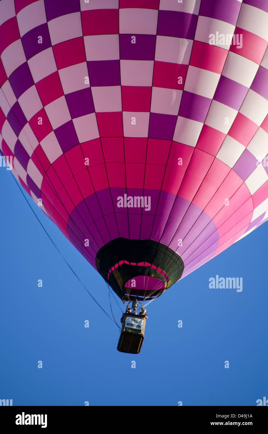 A cheerful pink-and-purple-checked hot air balloon rises into a clear ...