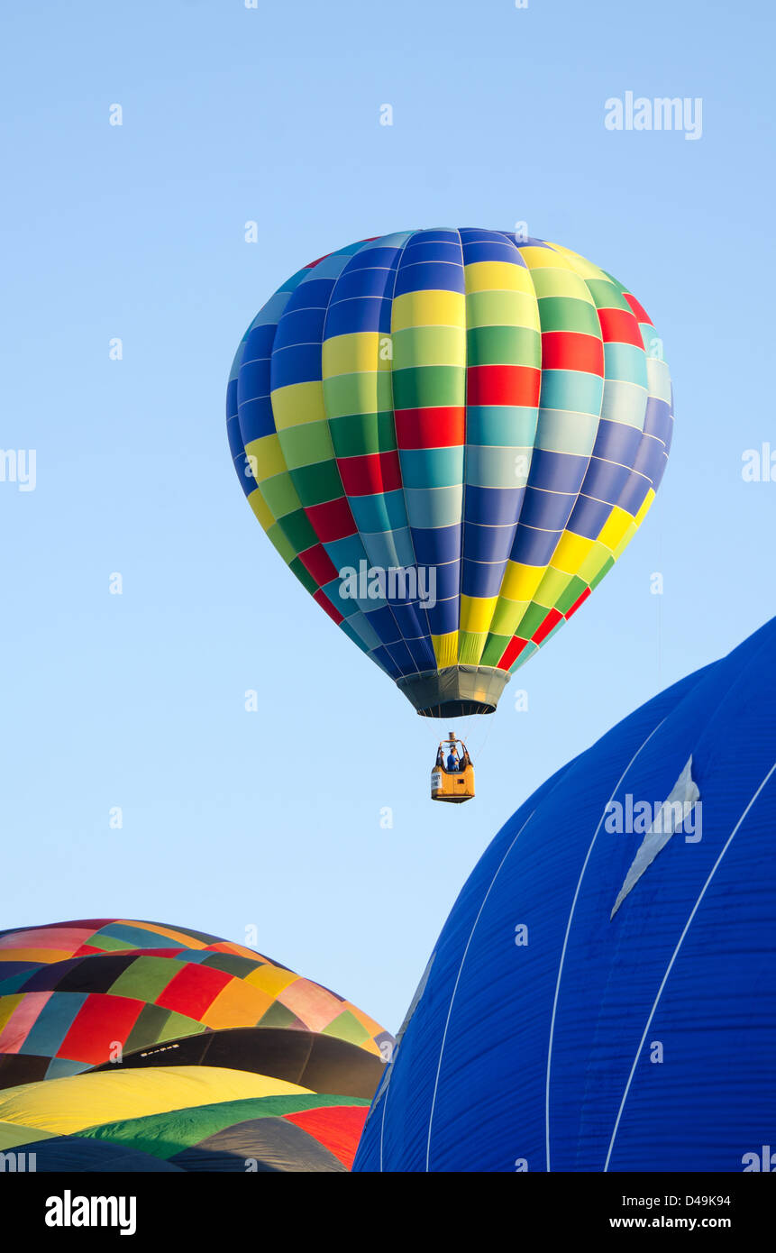 A brightly-coloured hot air balloon rises into a cloudless blue morning ...
