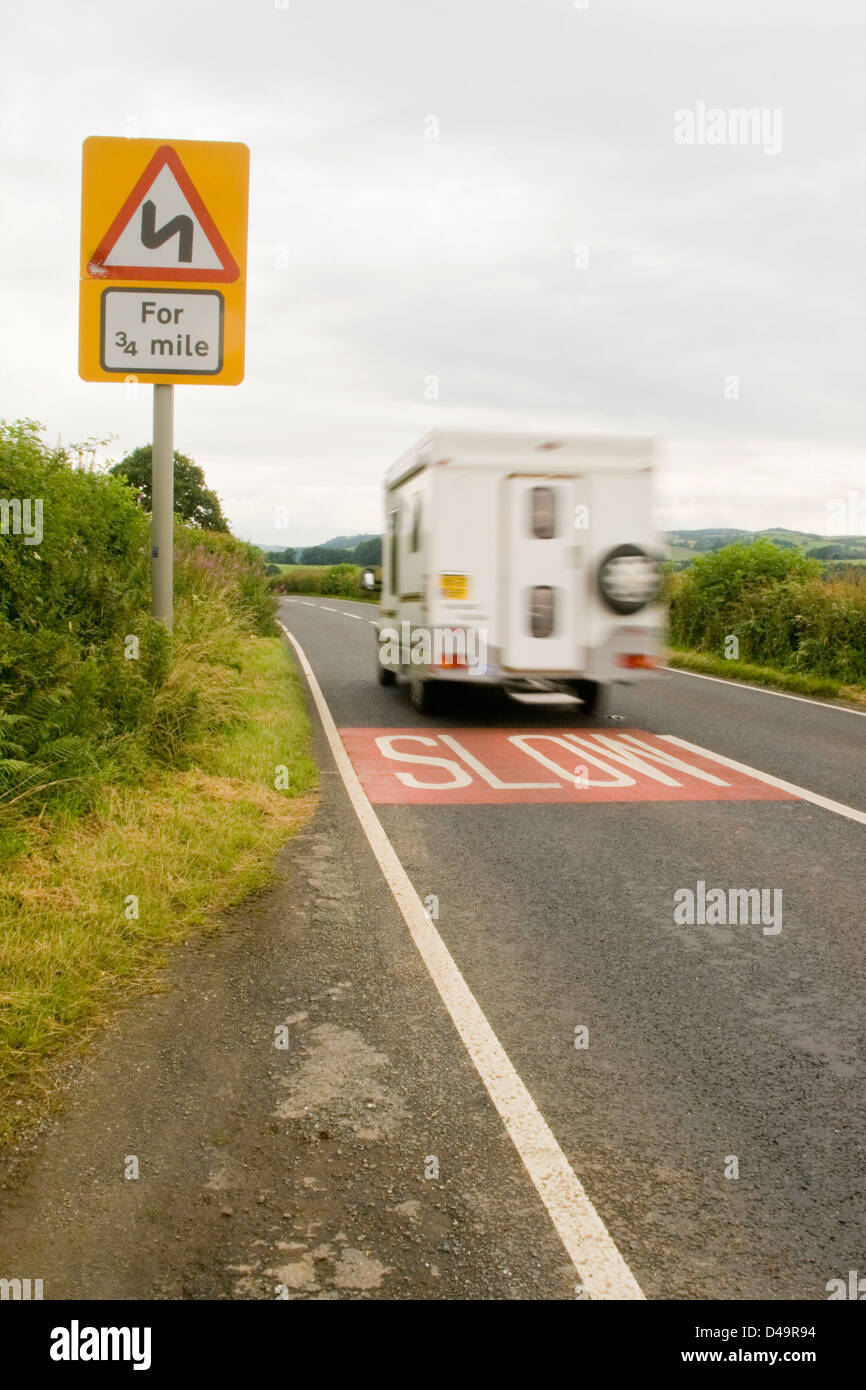 A Campervan traveling along a British countryside road past a Slow sign ...
