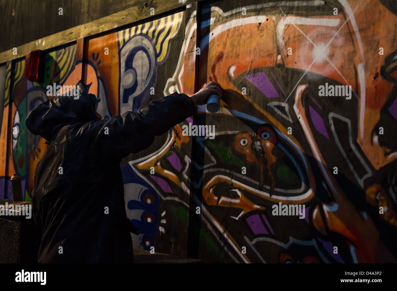 Graffiti on hoarding man in hooded top spraying graffiti hi-res stock ...