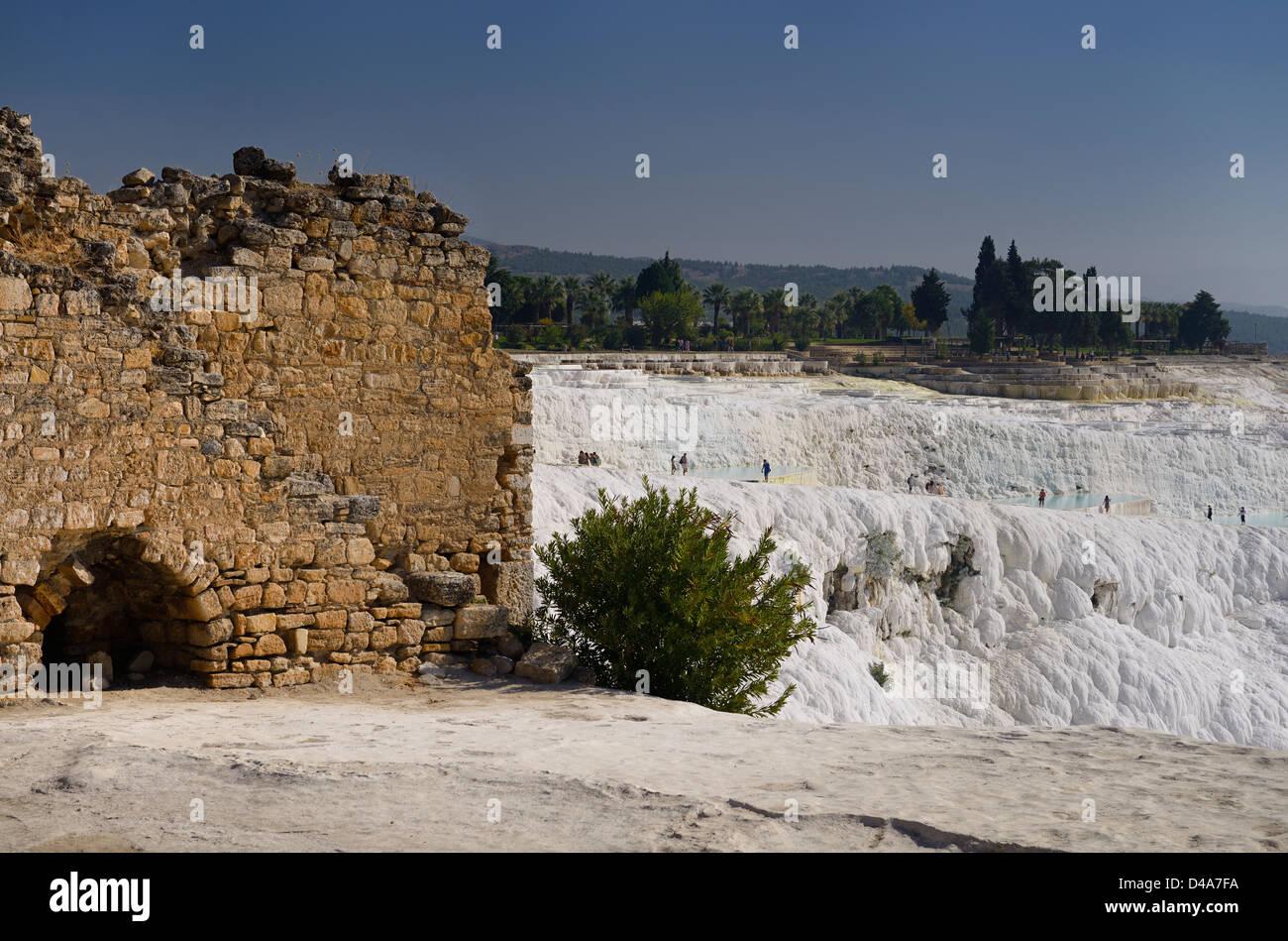 Ancient stone wall of Hierapolis ruins and tourists at thermal waters ...