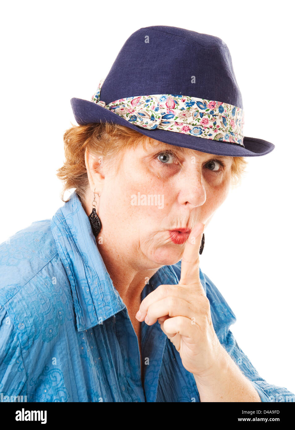 Middle-aged woman putting her finger to her lips in a hushing gesture ...