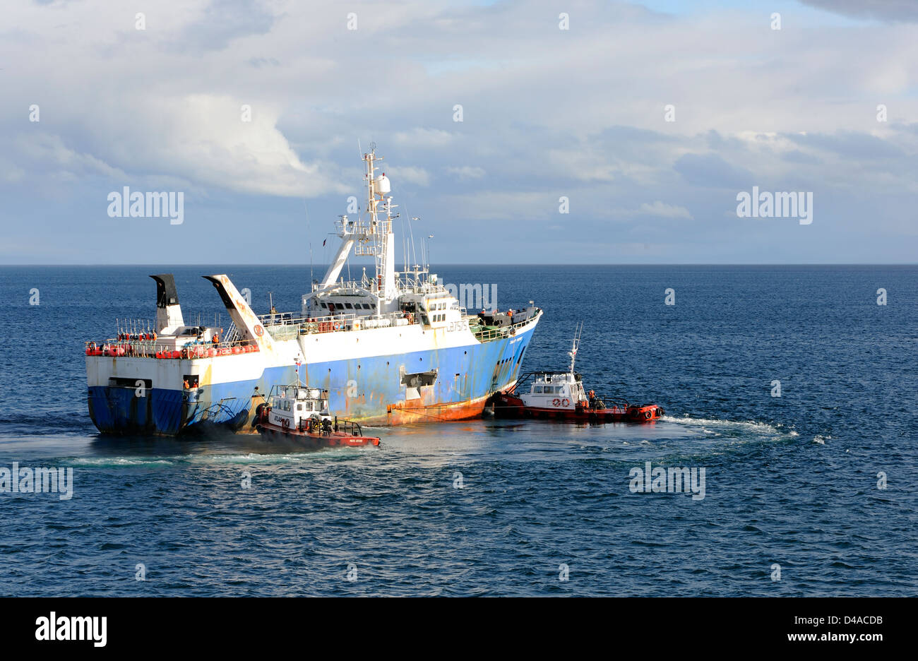 An ocean going fishing boat being manouvered by two tug boats in the ...