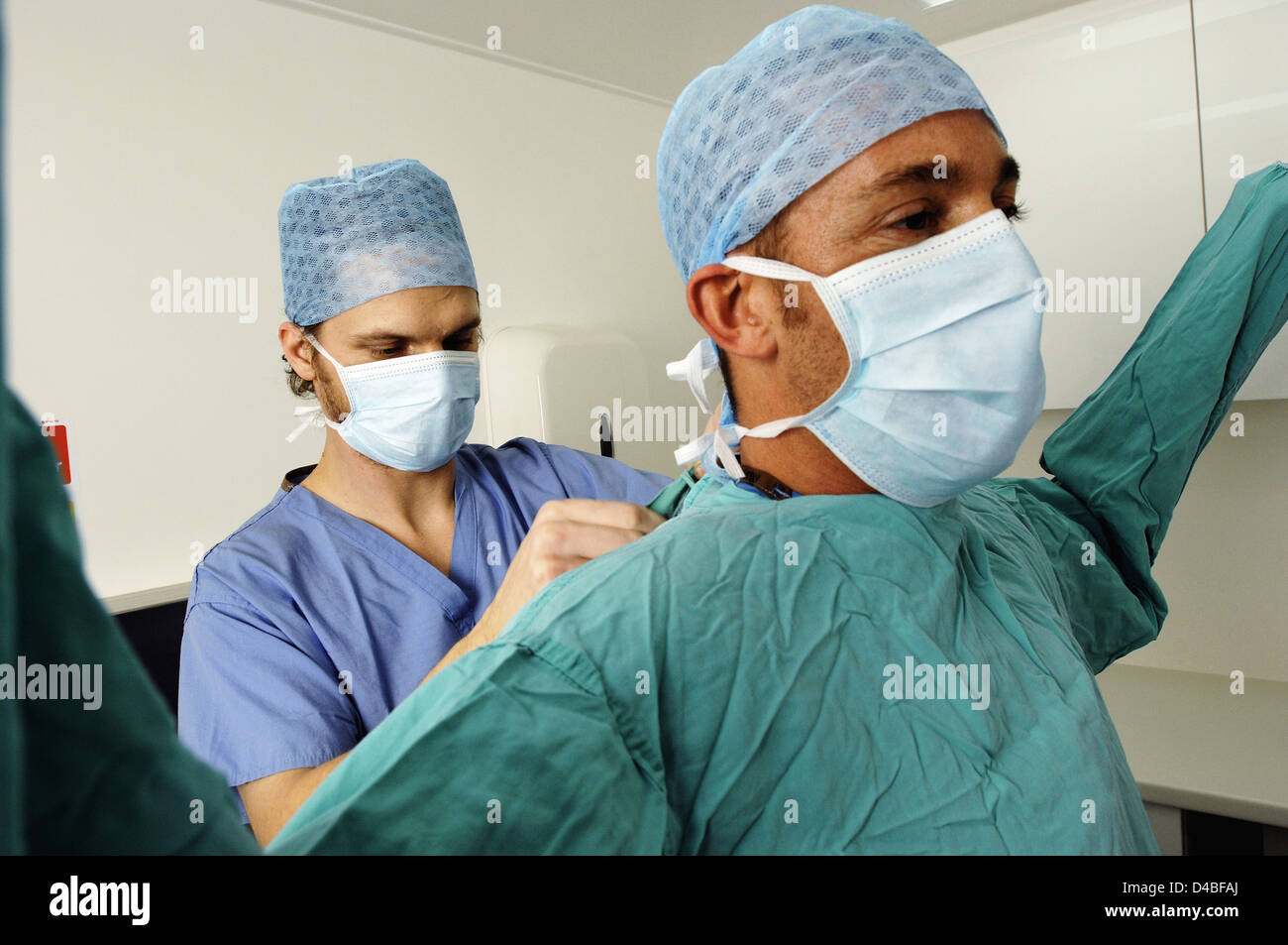 Operating theatre nurse is tying surgeons green surgical gown as they ...