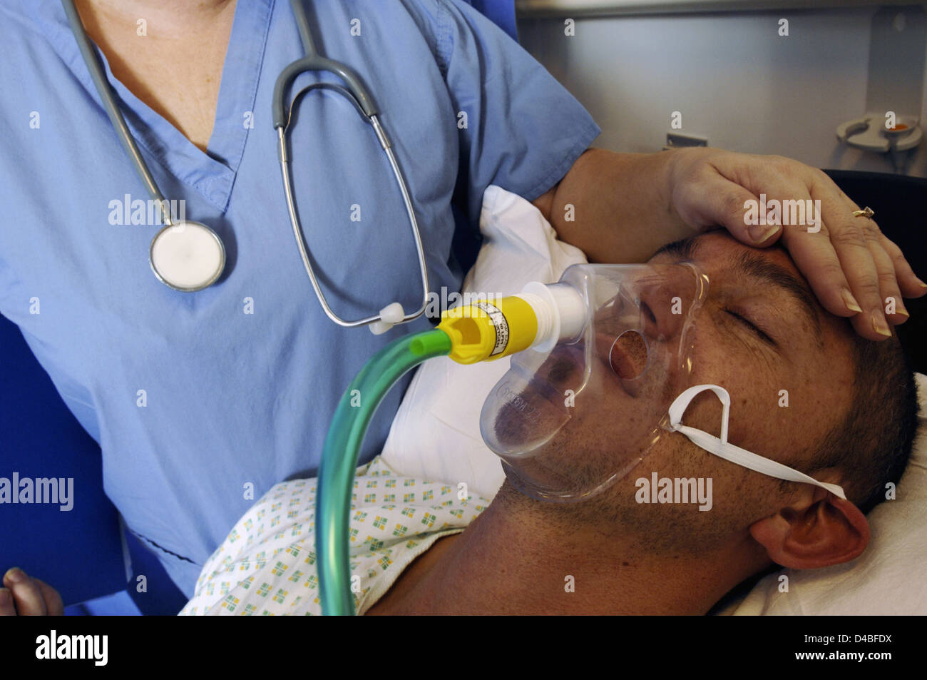 Close up of man wearing oxygen mask with nurses hand on his forehead ...