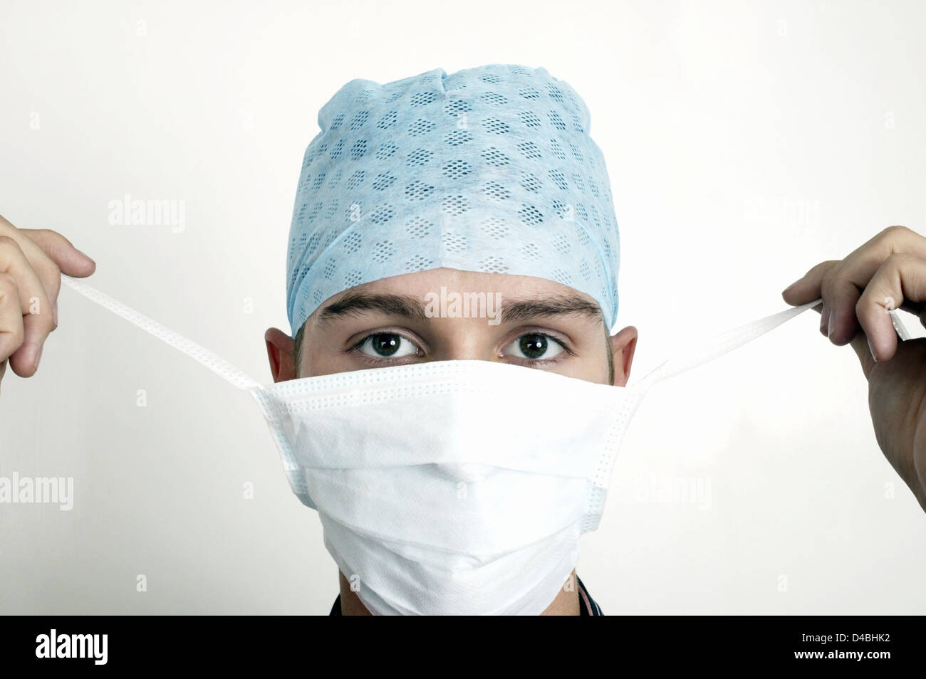 Close up of face of young doctor, wearing blue surgical cap and tying ...