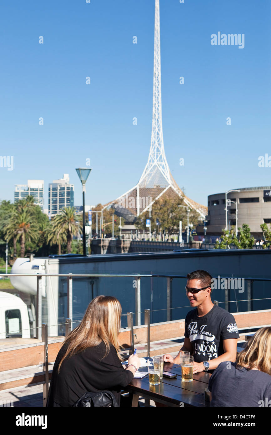 People relaxing at bar in Federation Square with spire of Victorian ...