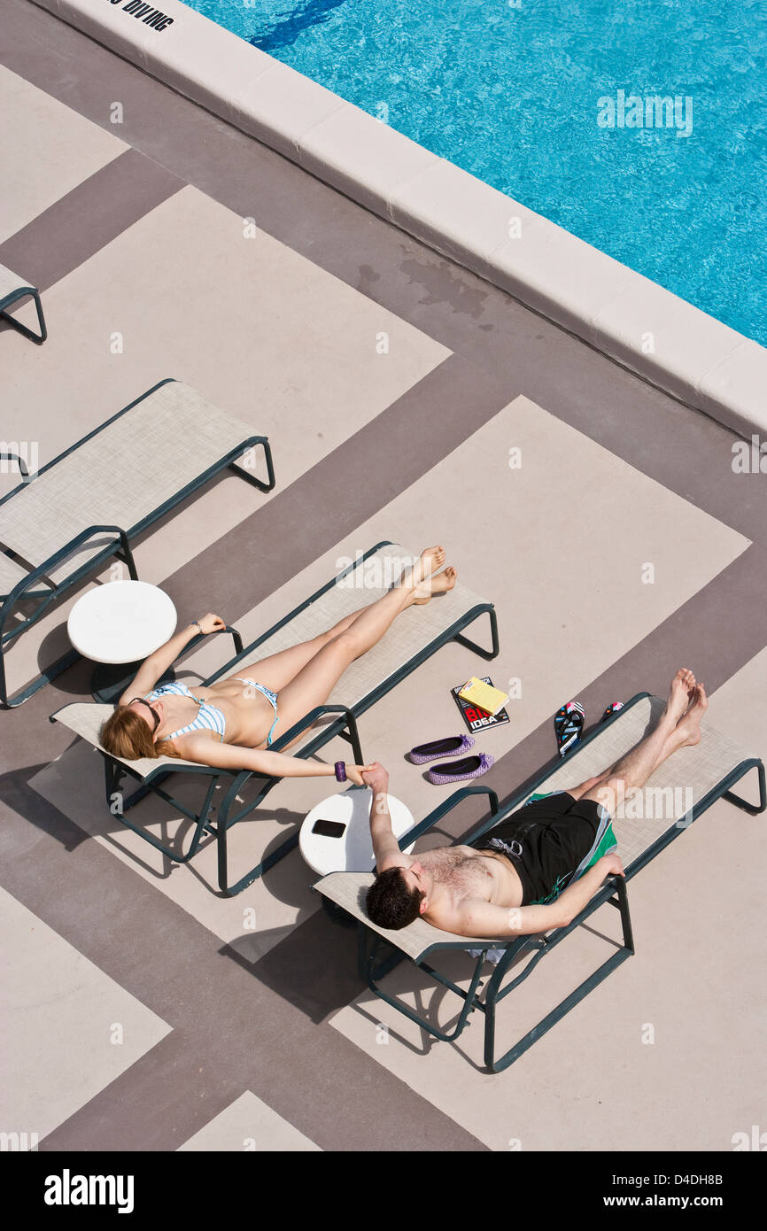 A young couple wearing bathing suits, holding hands, while relaxing on ...