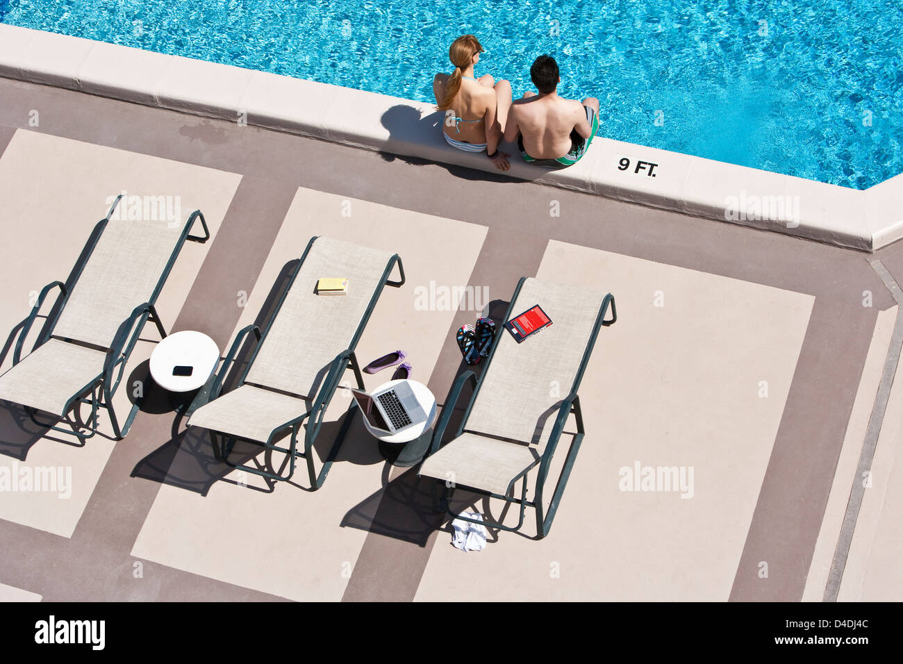 A young couple wearing bathing suits, sitting on the edge of a swimming ...