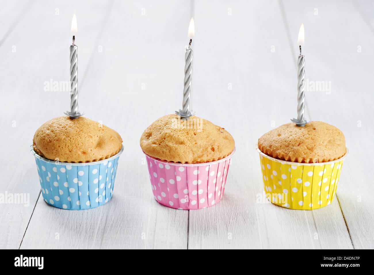 three muffins with candles in colorful muffin cases on white wooden ...