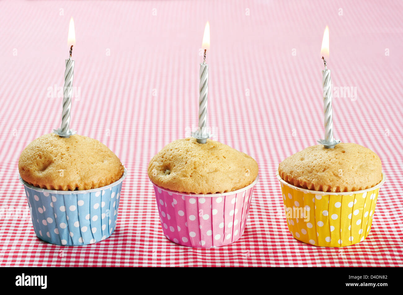 three muffins in colorful muffin cases with candles on red checkered ...