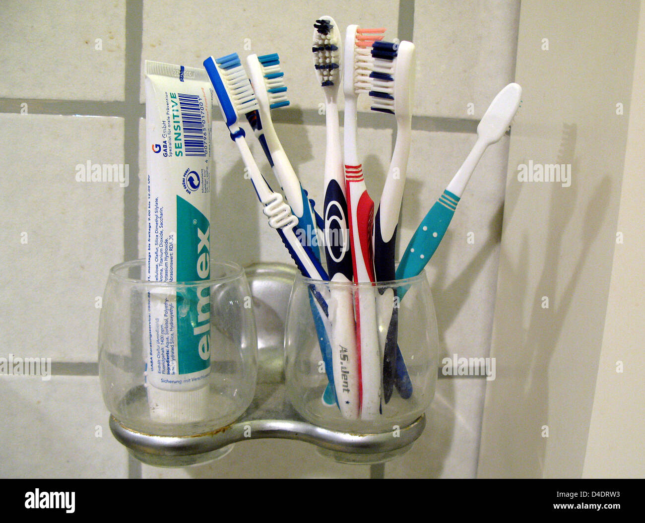 Seven tooth brushes and a tube of toothpaste share two glasses of a ...