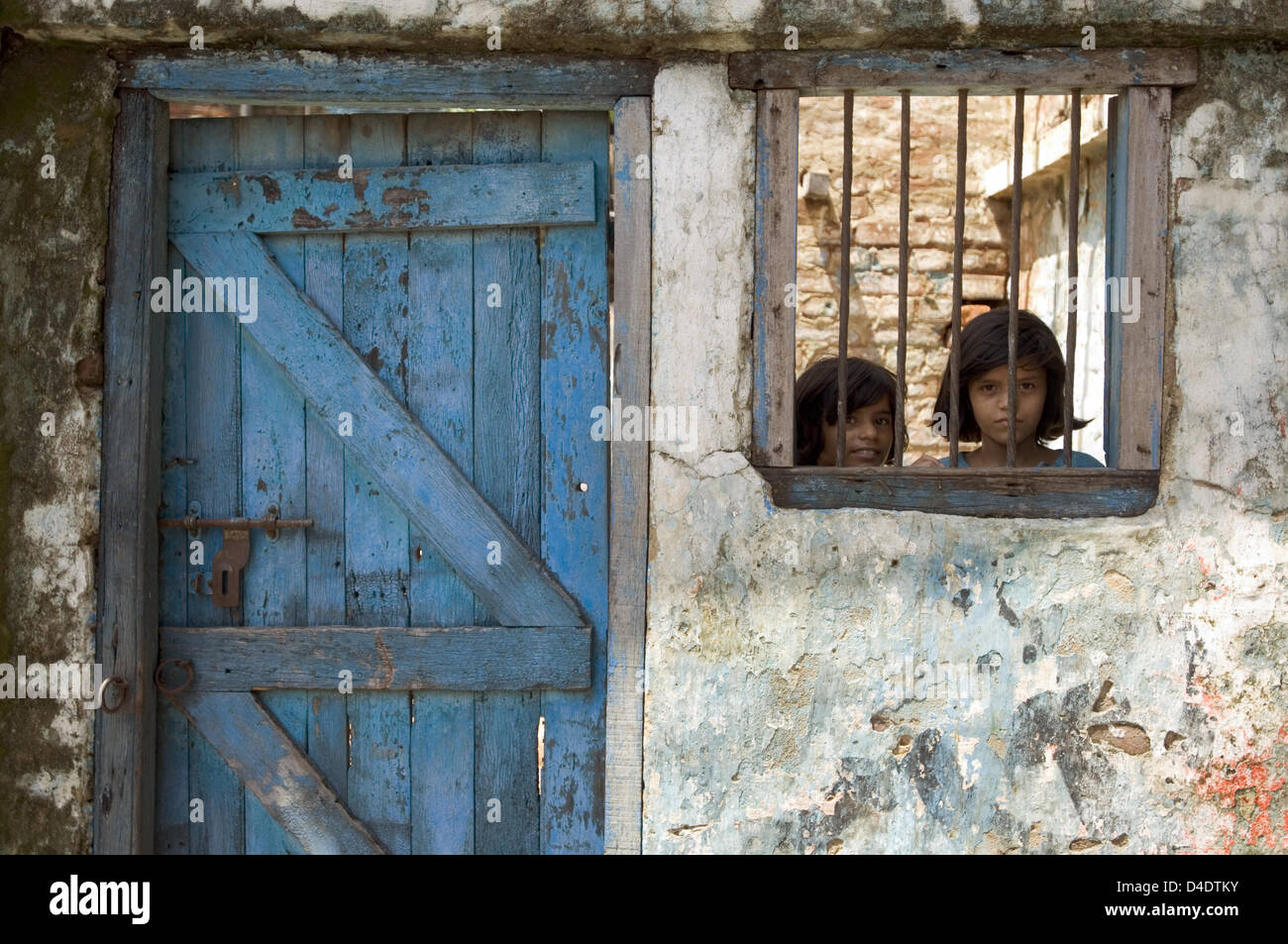 Two girls peek out a barred window in the slums of Pilkana in Howrah ...