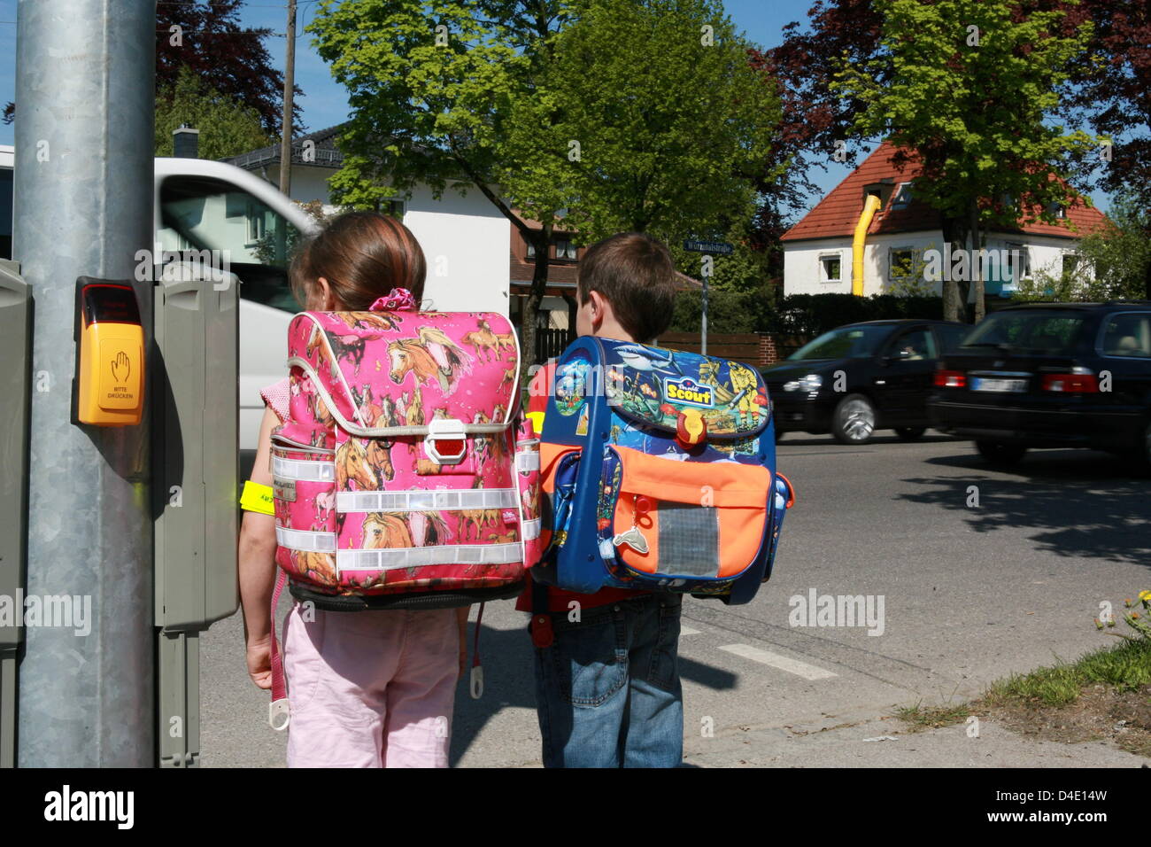 Two pupils with knapsacks on their backs wait at a traffic light on ...