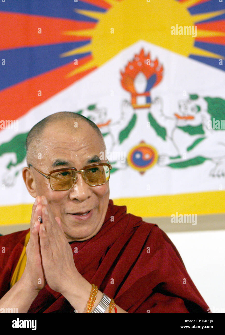 The Dalai Lama sits in front of a Tibetan flag and smiles during a ...