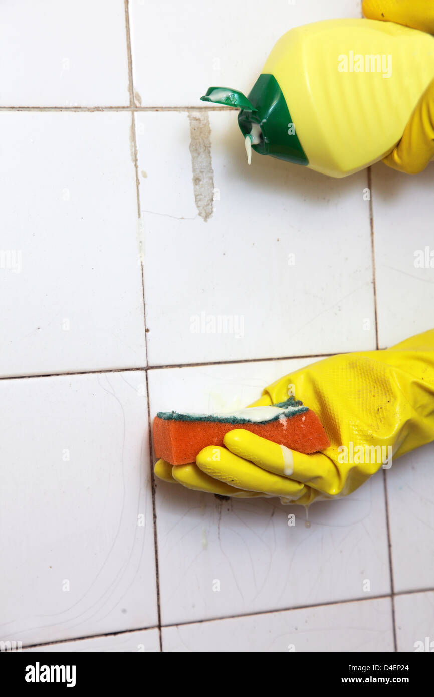 gloved hand cleaning dirty old tiles with sponge in a bathroom Stock ...