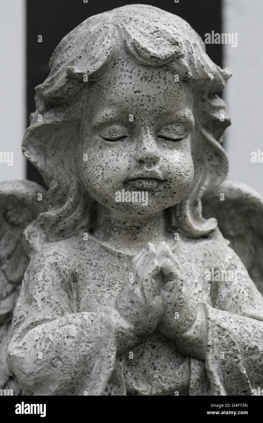 A stone sculpture resembling a praying angel with folded hands and ...
