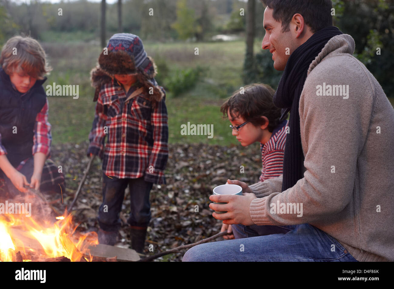 Father and children sitting around bonfire Stock Photo - Alamy