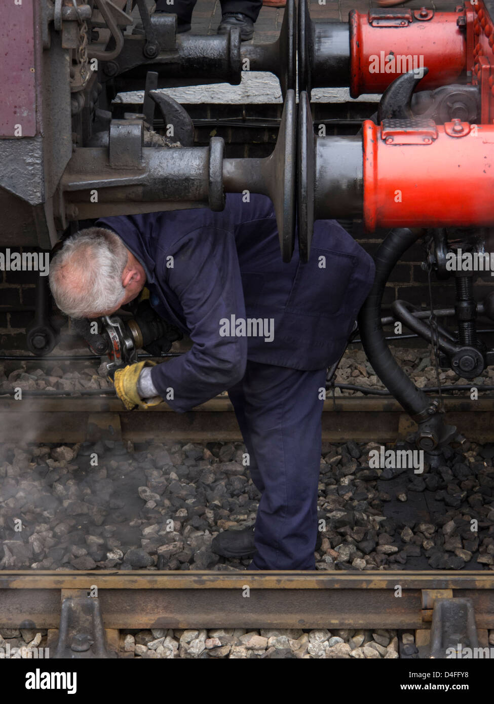 Train engineer connecting pipes on large steam train on the Poppy line ...