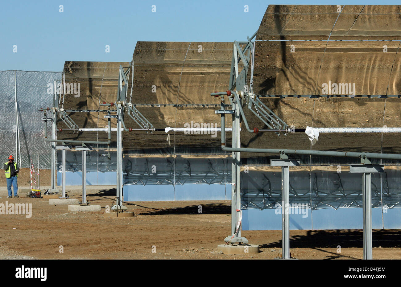 An engineer passes giant sunmirrors at the parabolic trough power plant ...