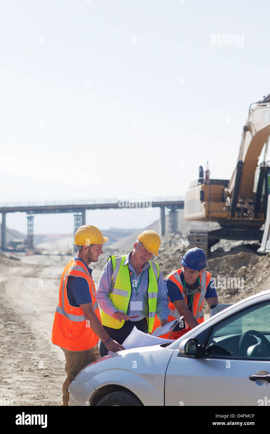 Three workers in a quarry discussing in front of heavy machinery Stock ...