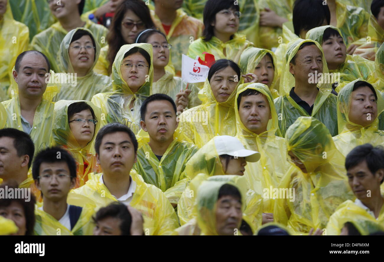 Spectators in raincoats sit on the grandstand to watch the womenÒs ...