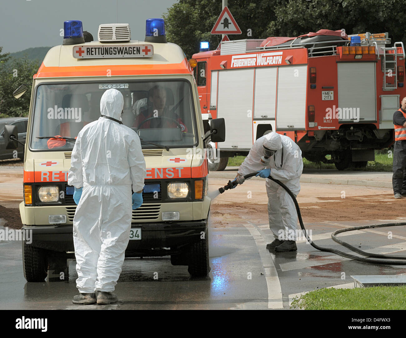 Firemen in protective suits hose down a vehicle with a high-pressure ...
