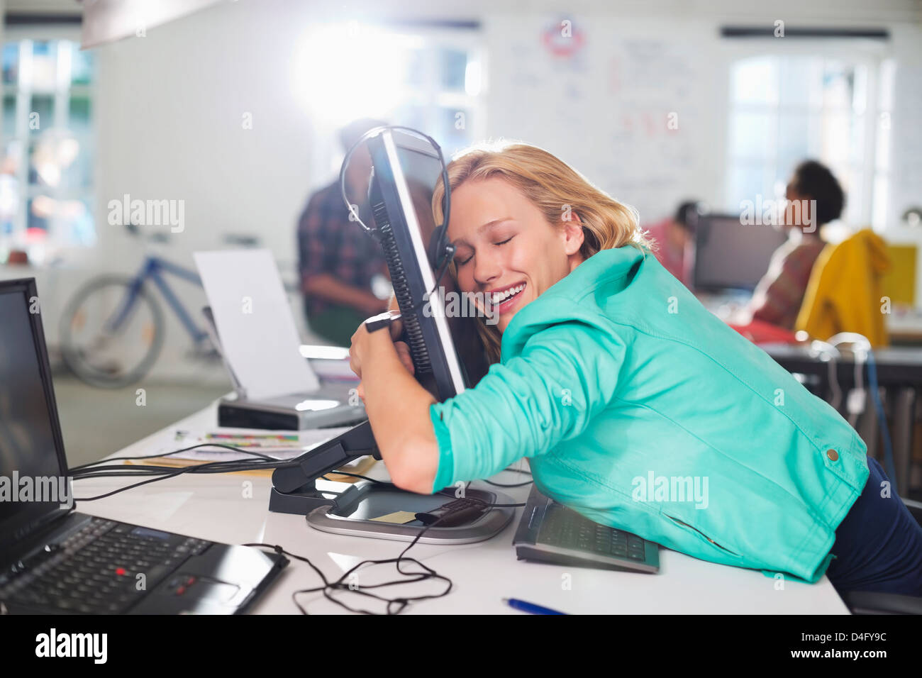 Businesswoman hugging computer at desk Stock Photo - Alamy
