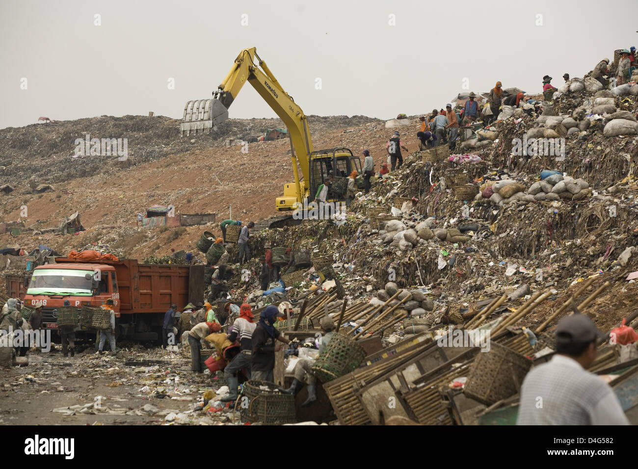Garbage collectors stand on a huge pile of rubbish, only a few ...