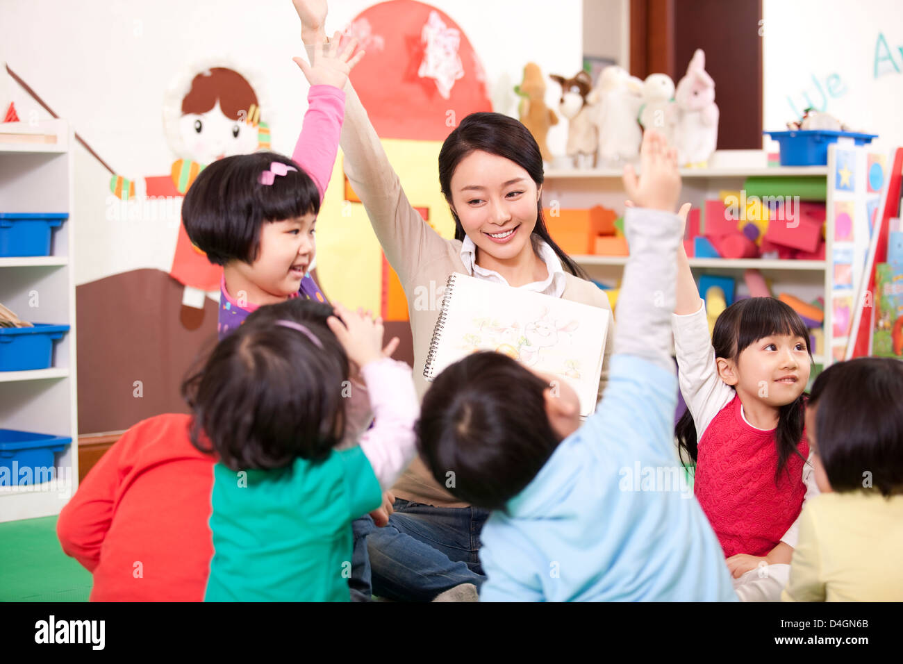 Cute kindergarten children raising hands to answer female teacher's ...