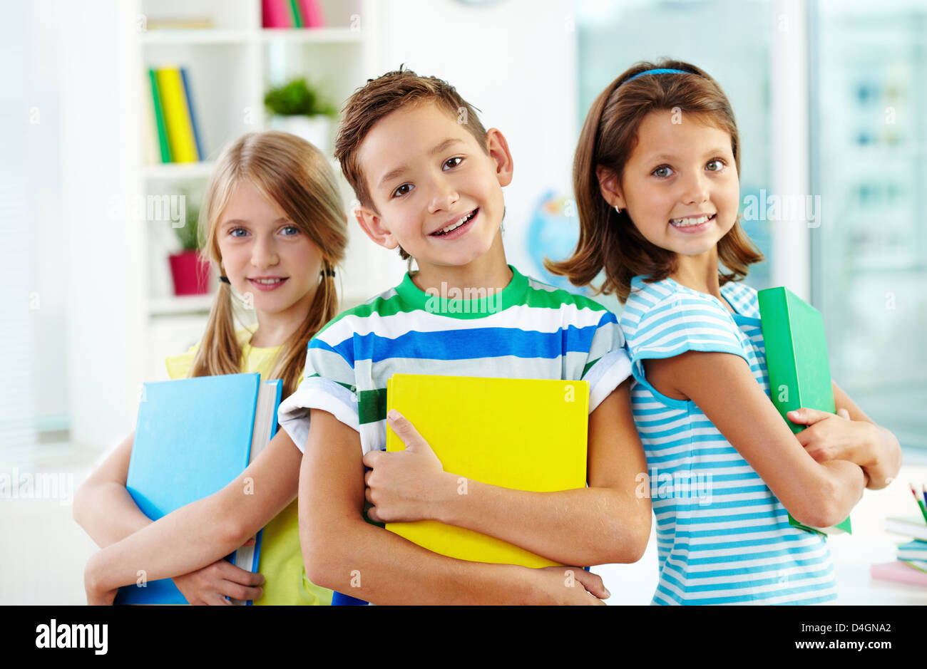 Portrait of happy classmates with books looking at camera in classroom ...