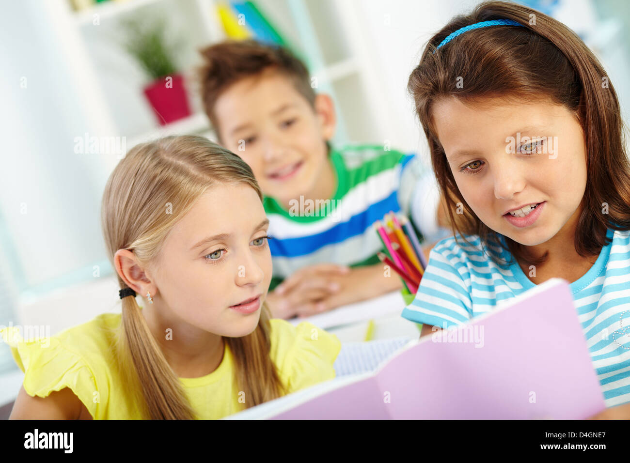 Portrait of lovely schoolgirls reading with schoolmate on background ...