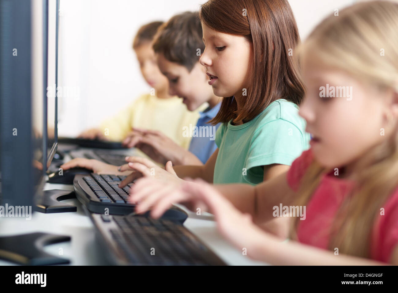 Portrait of lovely schoolgirl looking at computer keyboard while typing ...