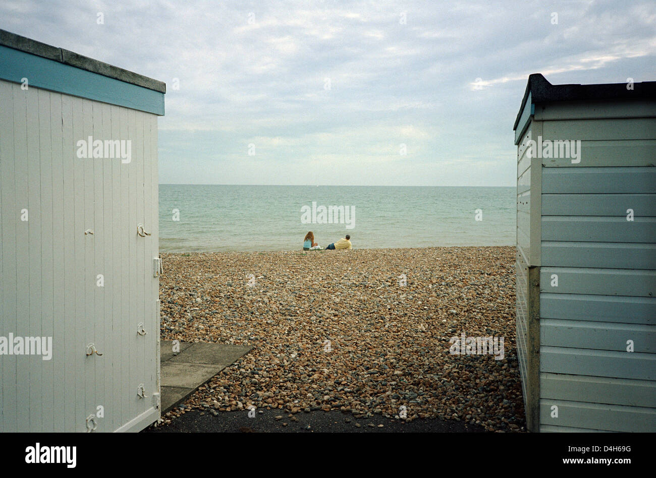 Couple sunbathing on beach between two beach huts Stock Photo - Alamy
