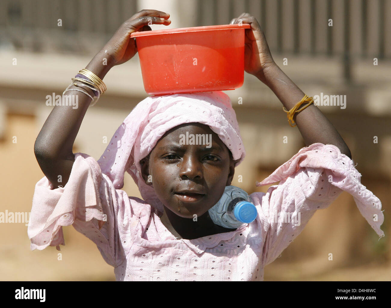 A Nigerian girl carries a red bowl on her head at Wuse-market in Abuja ...