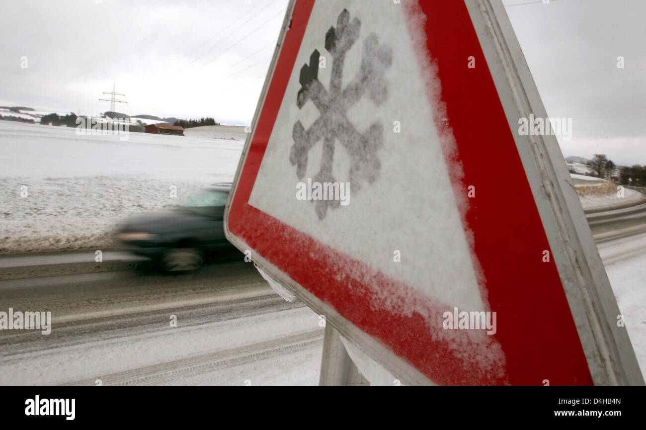 A road sign warning of black ice and snow is covered in snow in ...