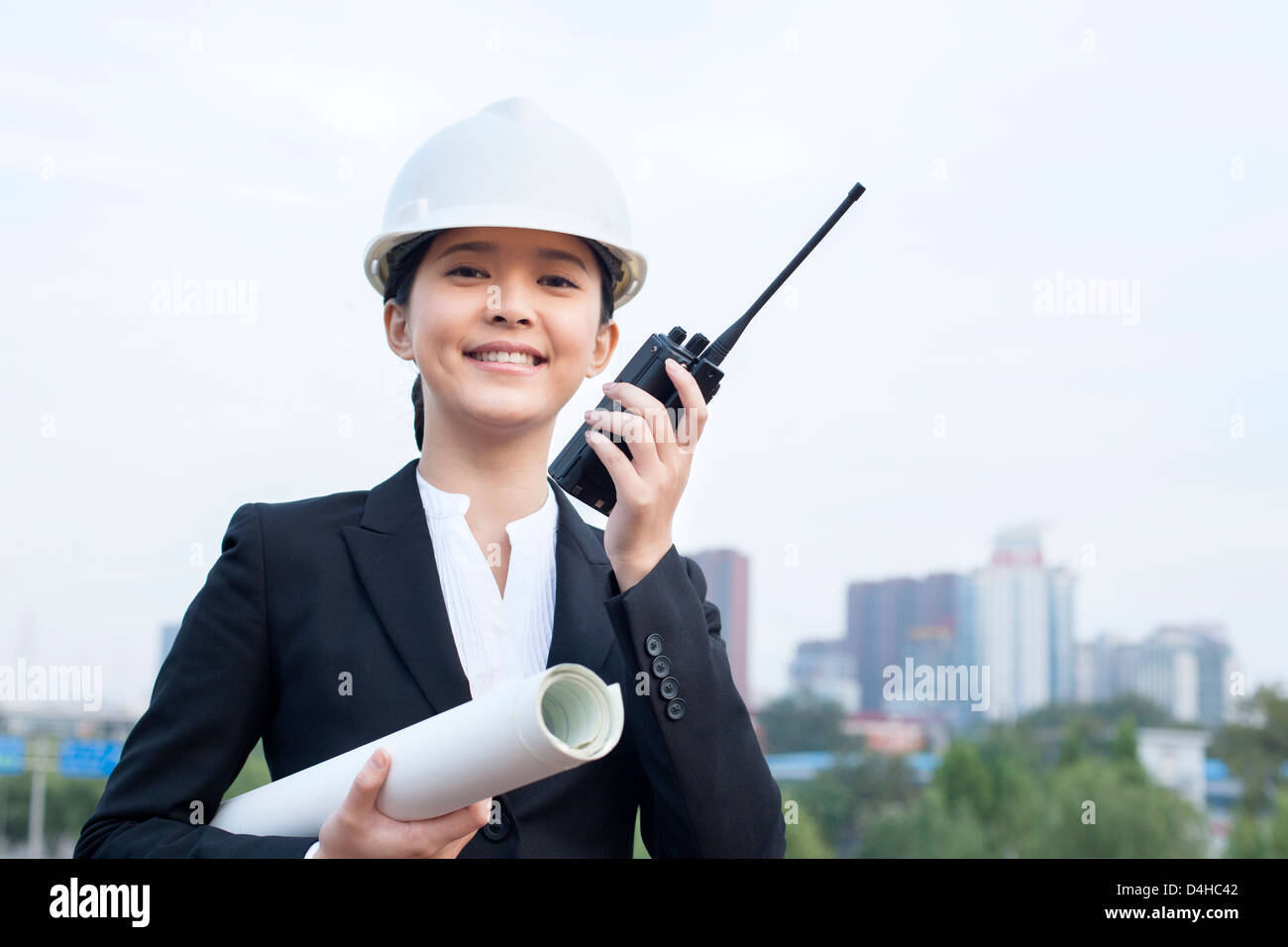 Young female architect with intercom and blueprint outdoors Stock Photo ...