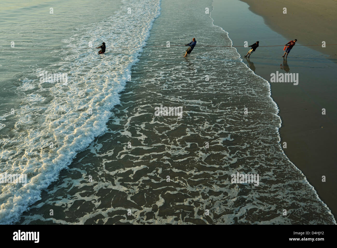 Early morning scene of four men pulling rope of fishing net in shallow ...