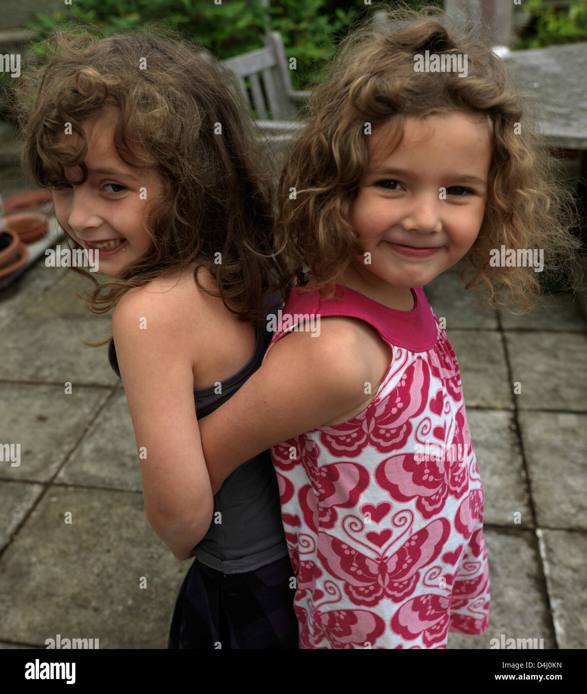 Sisters Back To Back Linking Arms In The Garden England Stock Photo - Alamy