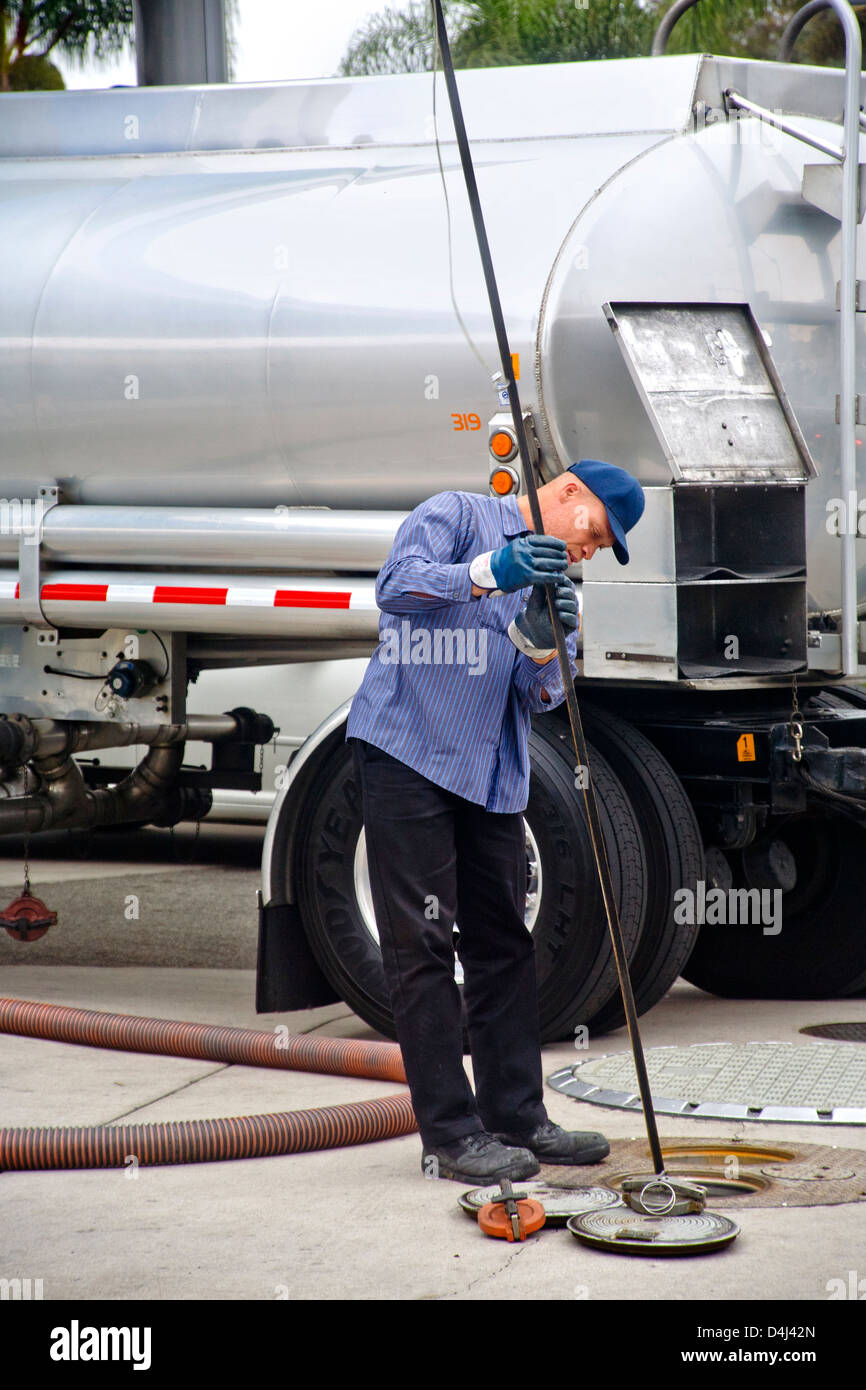 Using a long dip stick, a gasoline delivery man measures the levels in ...