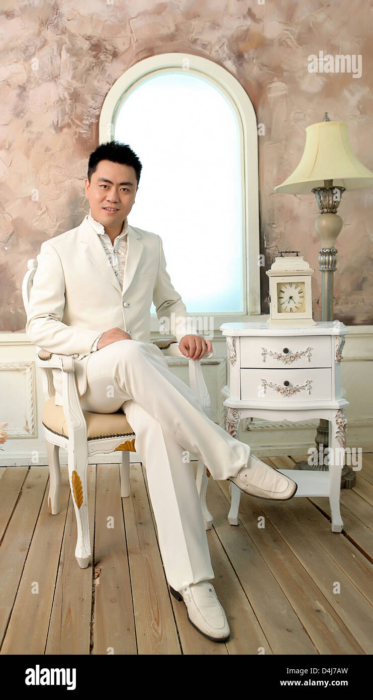 Chinese young man in white suite sitting in chair in bright room Stock ...
