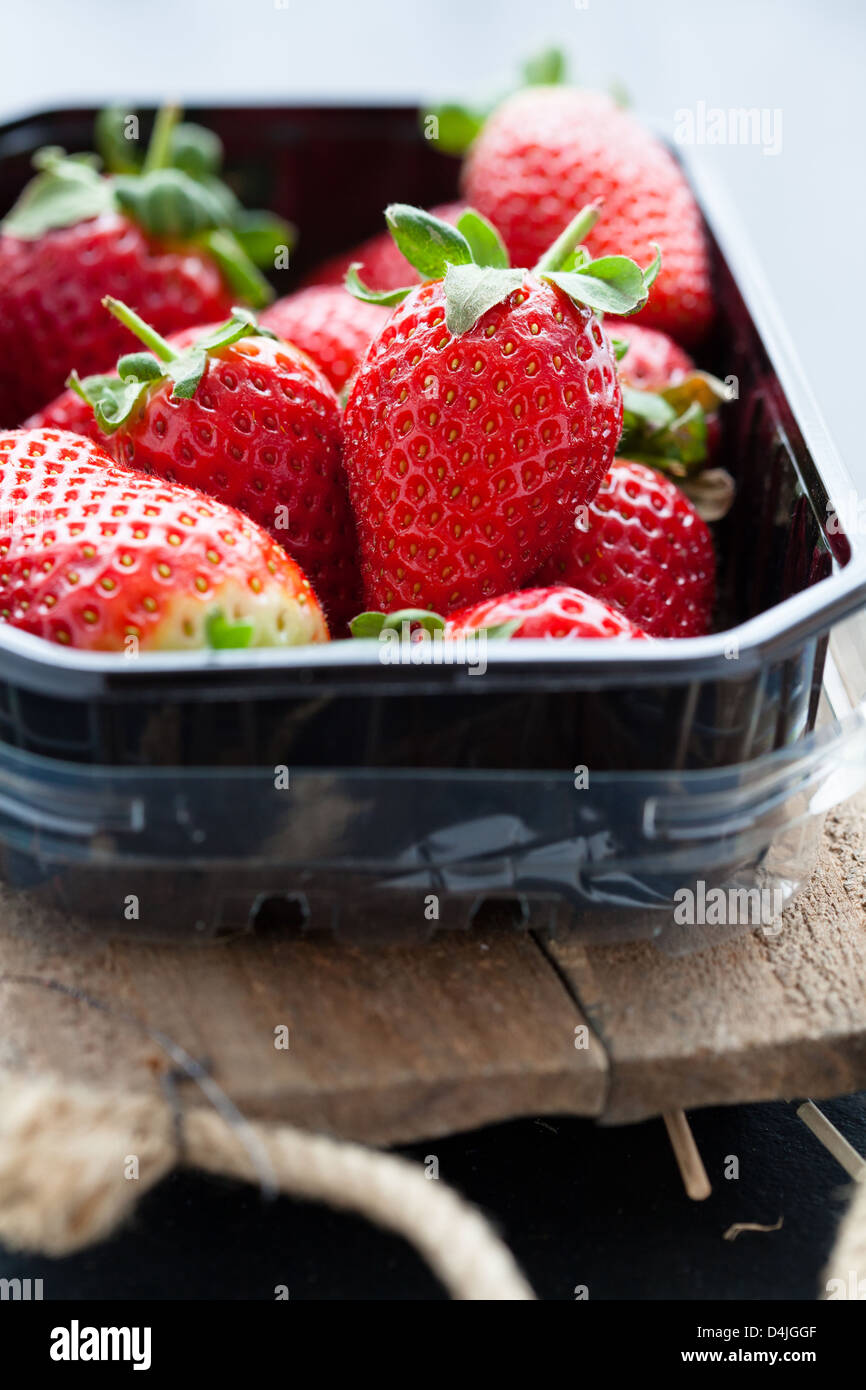 Fresh whole strawberries in plastic packing tray on wooden surface ...