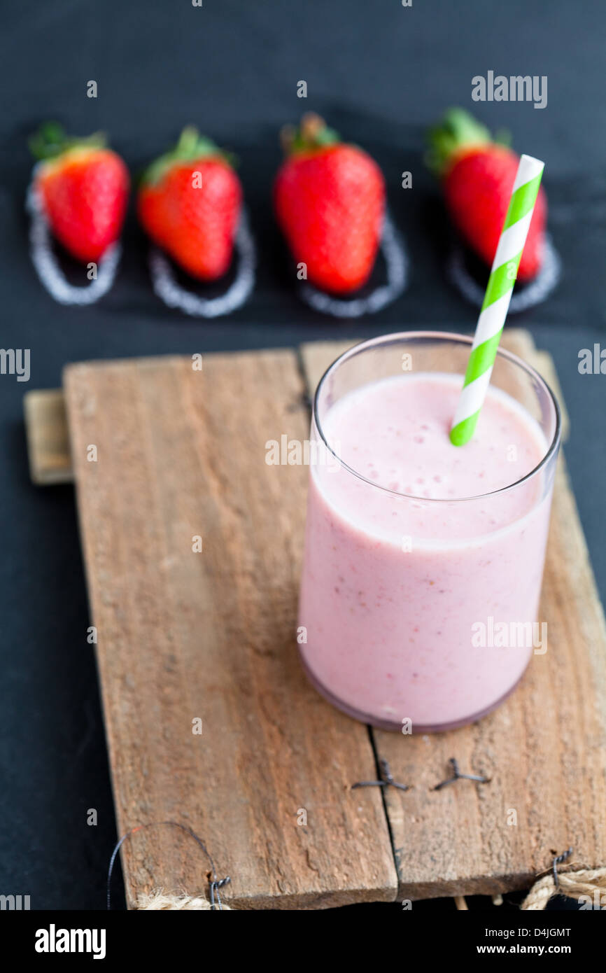Strawberry smoothie with striped straw and whole strawberries on dark ...