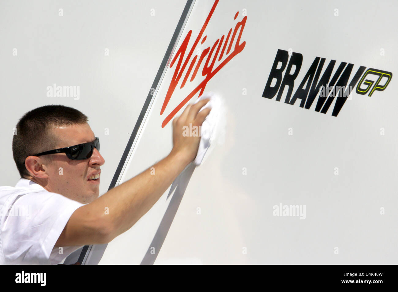 A Brawn GP mechanic cleans a sign showing logos of the new partners ...