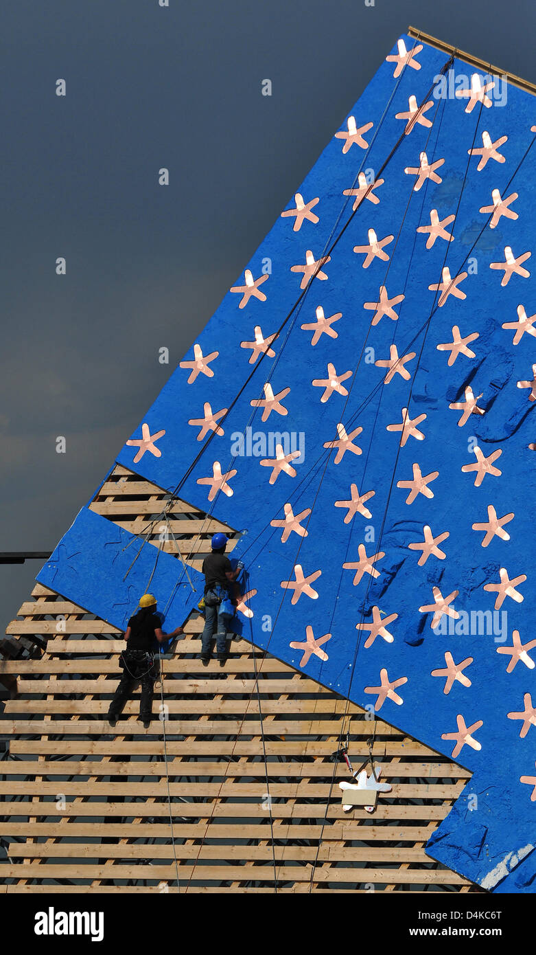 Two workers who are secured by ropes assemble a part of the stage ...