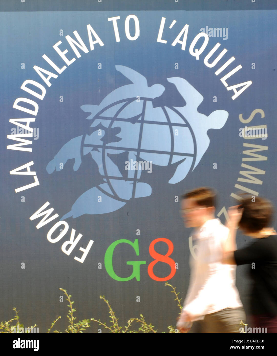 Journalists walk past the logo of the G8 summit 2009 at the press ...